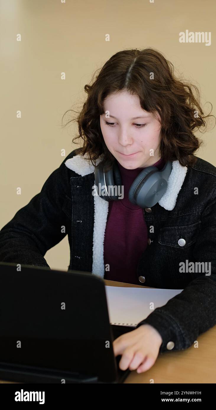 A thoughtful girl sits with headphones around her neck and a laptop in ...