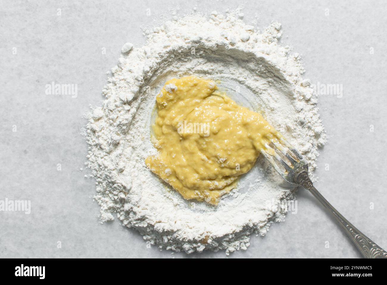 Overhead view of flour and egg being mixed on a white countertop, top ...