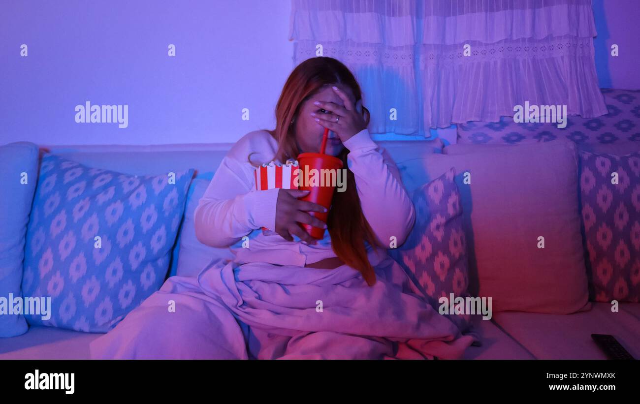Scared woman covering herself in fear while watching horror movie ...