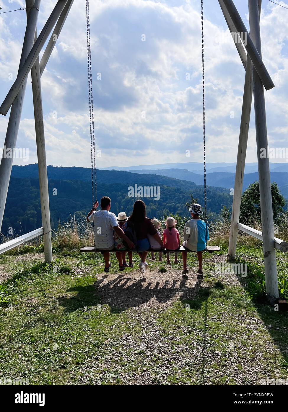 A group of people sitting on a large swing, enjoying a picturesque ...