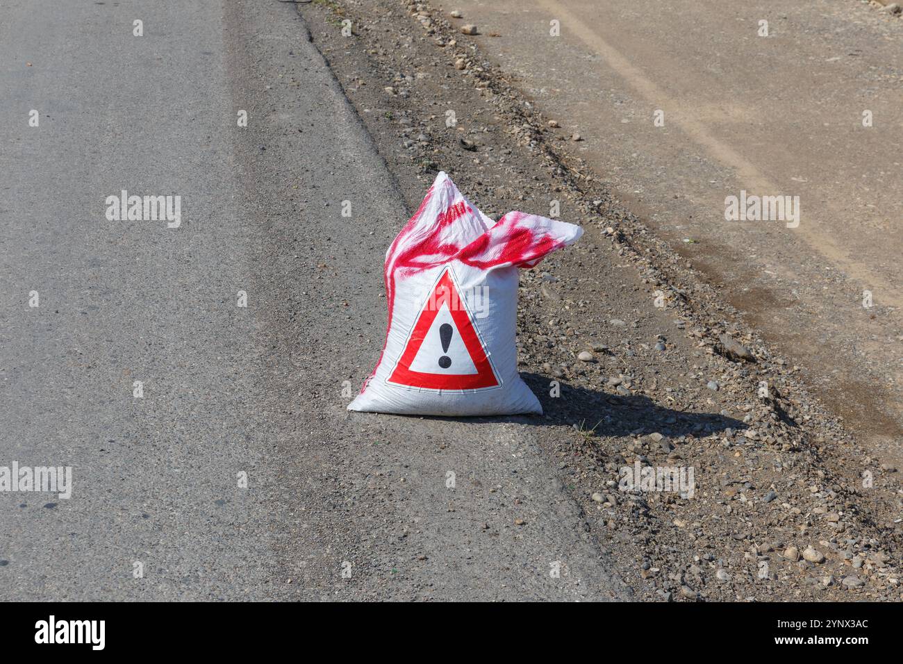A bag marked with a warning sign sits by the roadside, suggesting ...