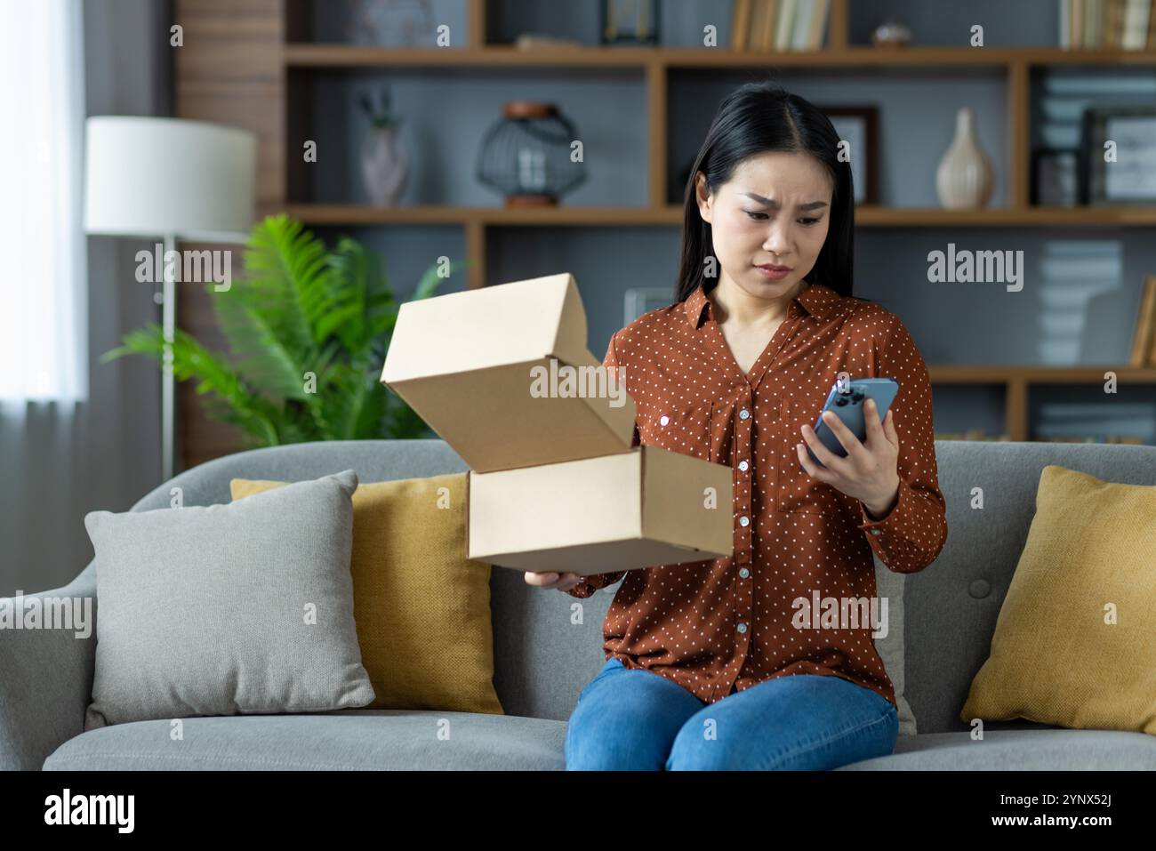 Asian woman at home with phone handling cardboard boxes, appearing ...