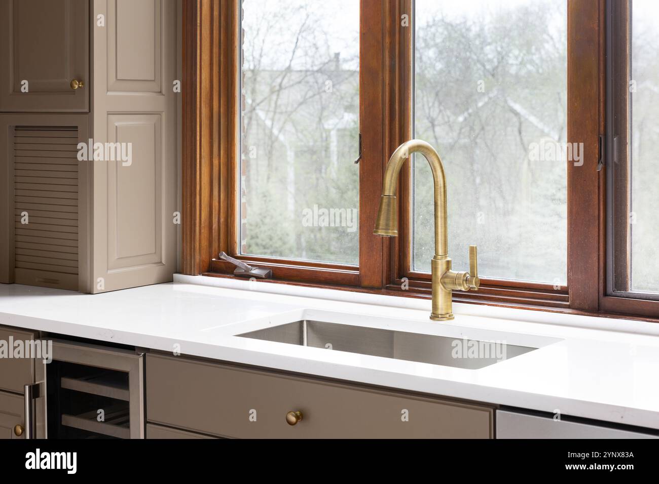 A gold kitchen faucet detail with brown cabinets, wood frame windows ...