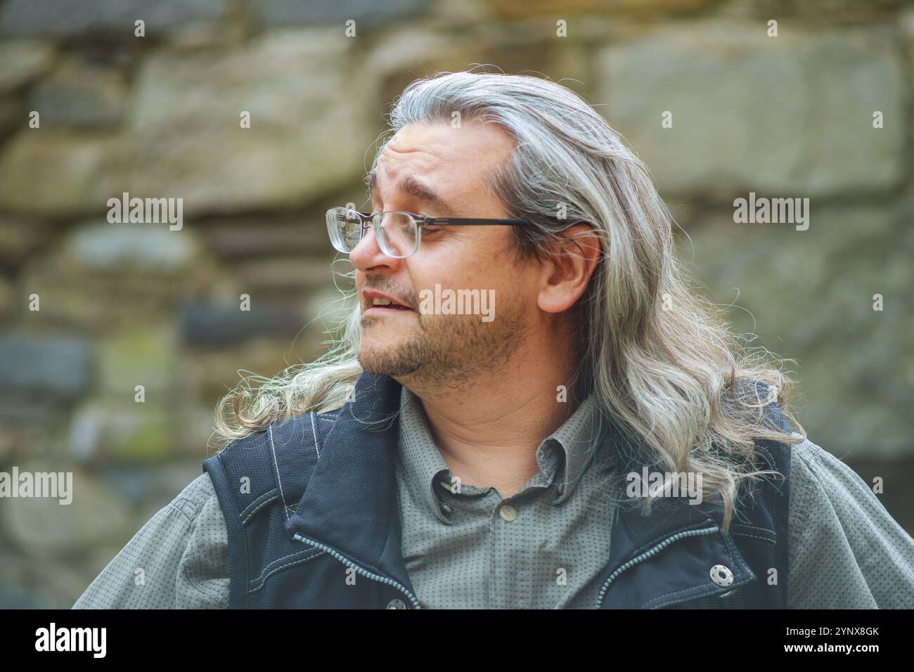 Man with long, silver hair glasses stands faced slightly away from ...