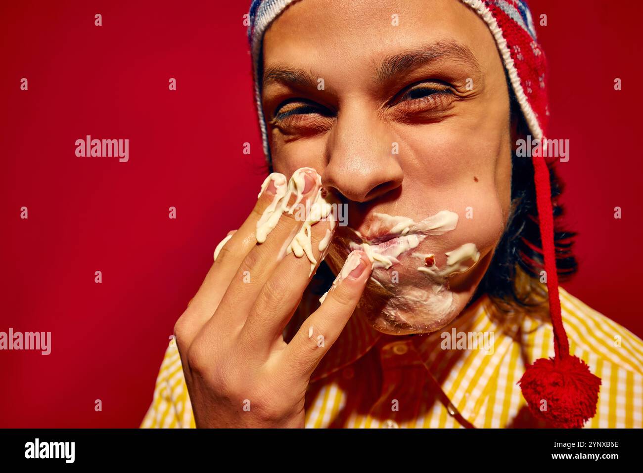 Delicious messy bite. Young man in winter hat, with face covered in ...