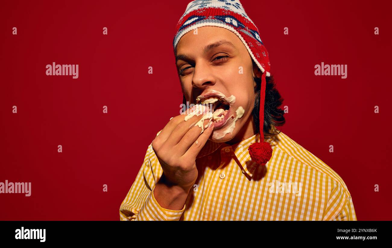Delicious messy bite. Young man in winter hat, with face covered in ...