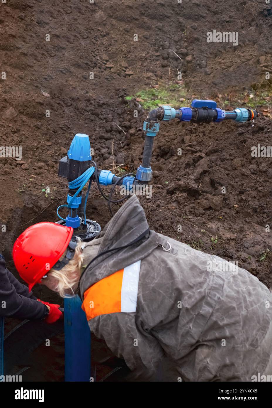 Workers install a water intake unit in a well. Installation of the ...