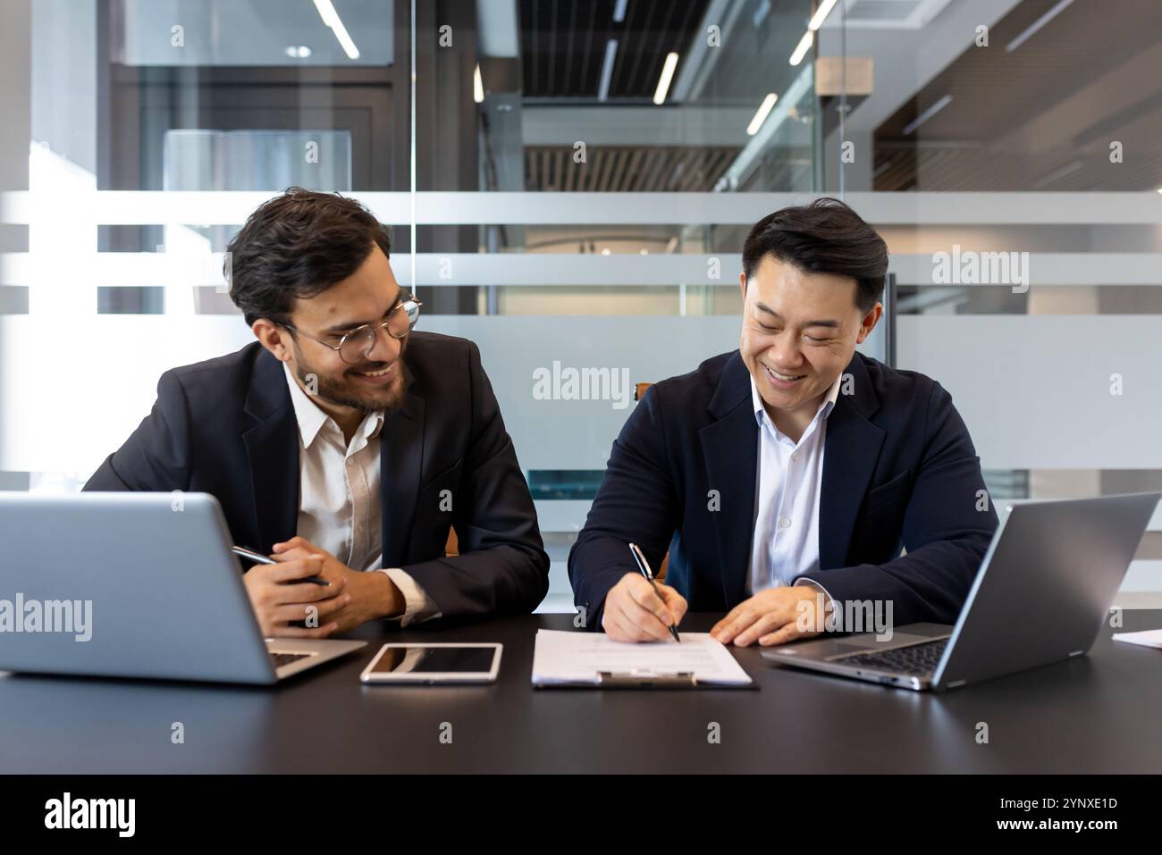Businessmen in office signing consent agreement with laptops and phone ...