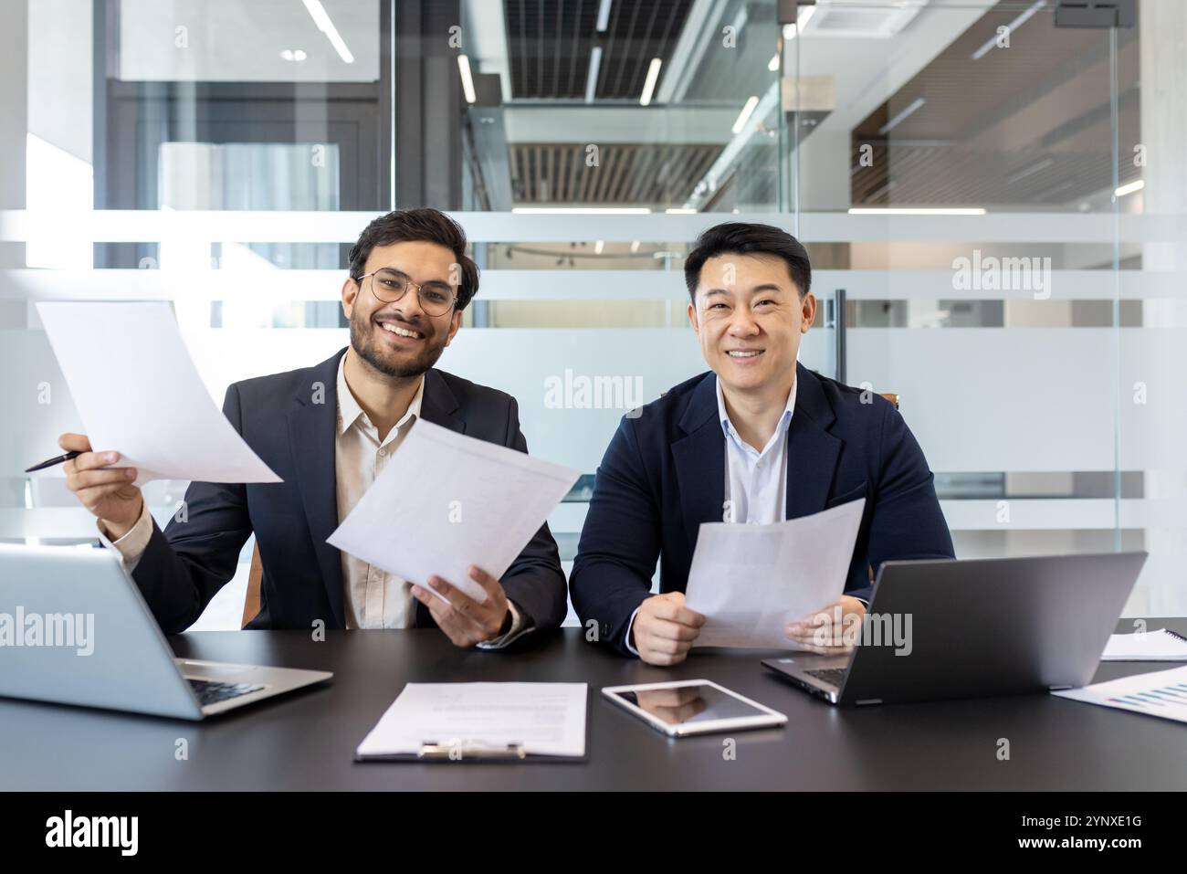 Smiling businessmen seated at office desk holding documents ...