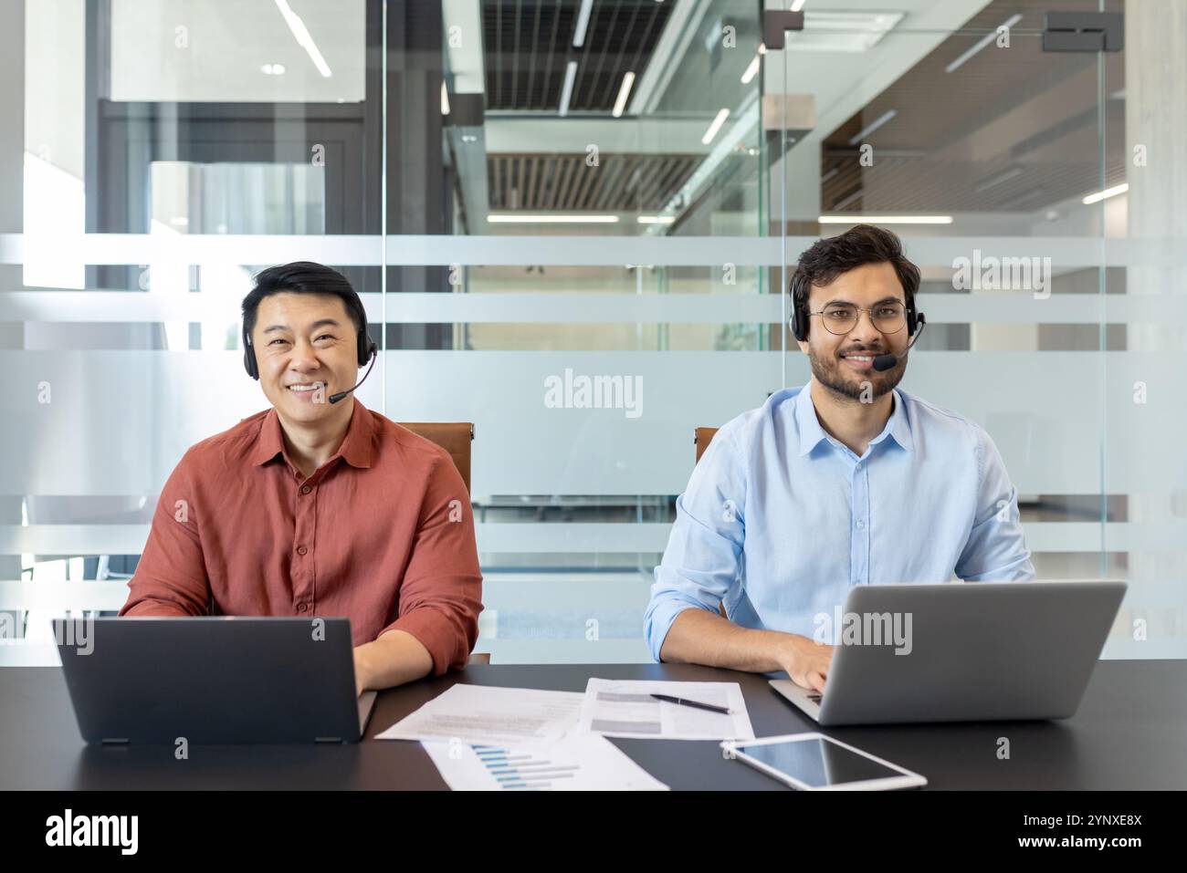 Two male customer service professionals with headsets work at laptops ...