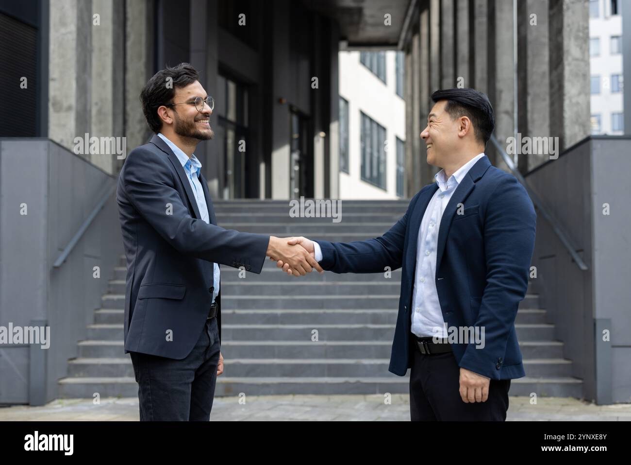 Businessmen shaking hands outside modern building, symbolizing ...
