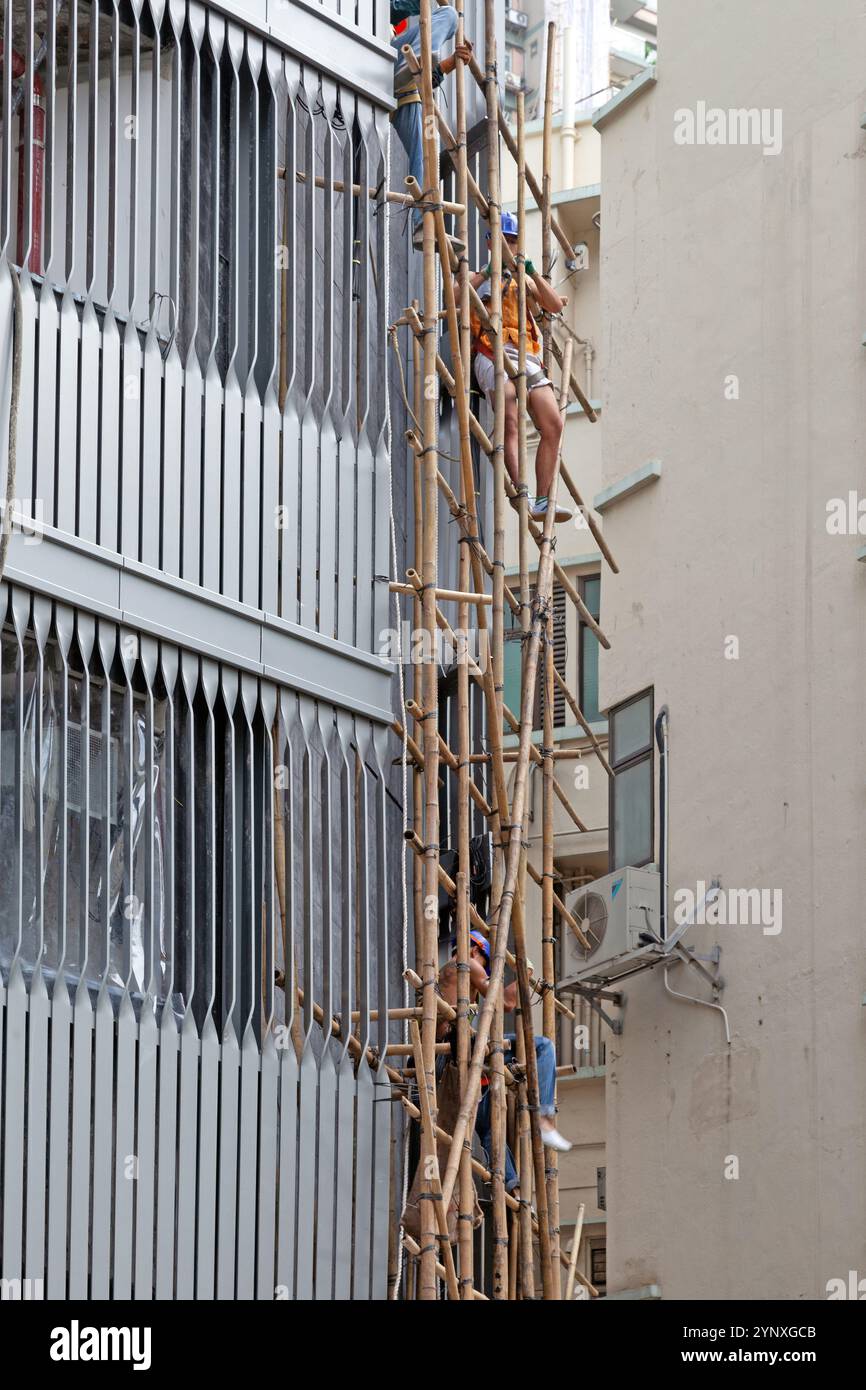 Workers climbing bamboo scaffolding on a modern building, showcasing ...