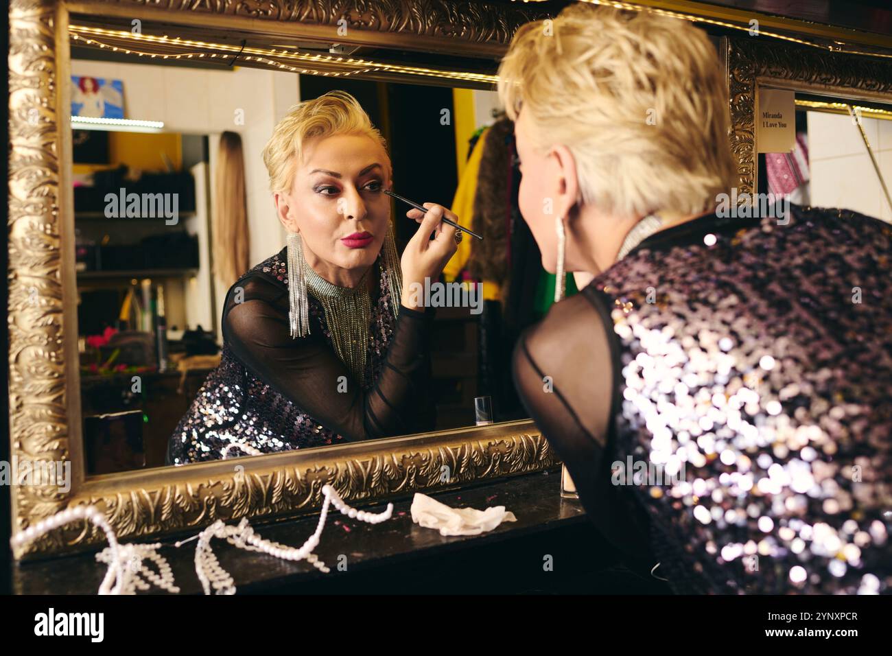 In a lively dressing room, a drag queen applies stunning makeup before ...