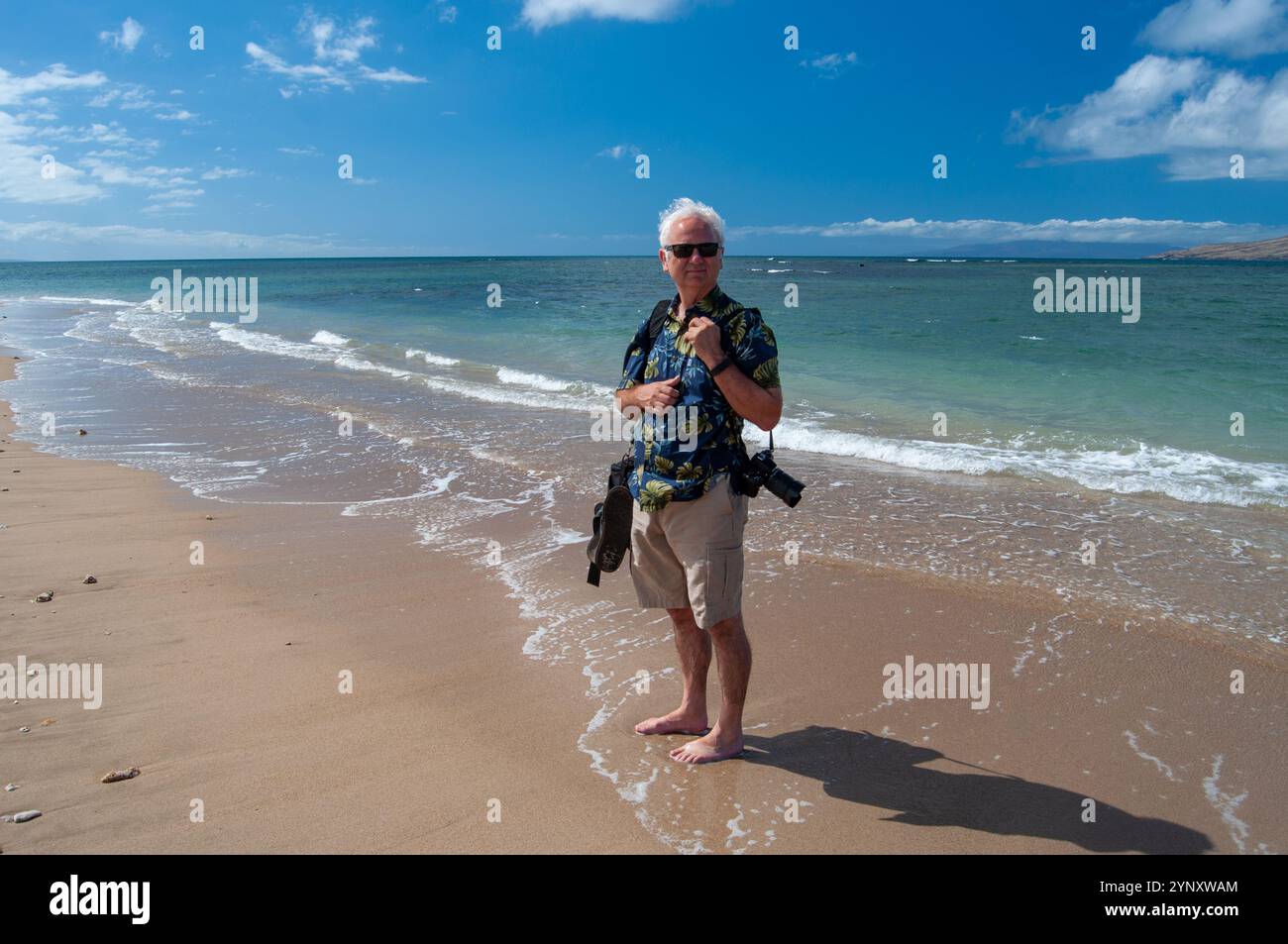 Smiling Barefoot man with a camera standing in ocean surf on a beach ...
