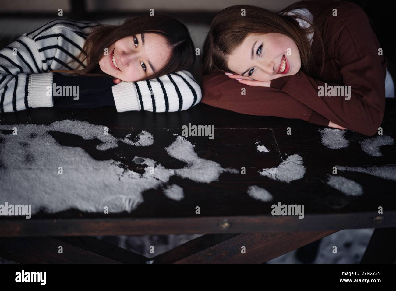Two young schoolgirls are lying on a snow covered table, enjoying a winter photoshoot outdoors ...