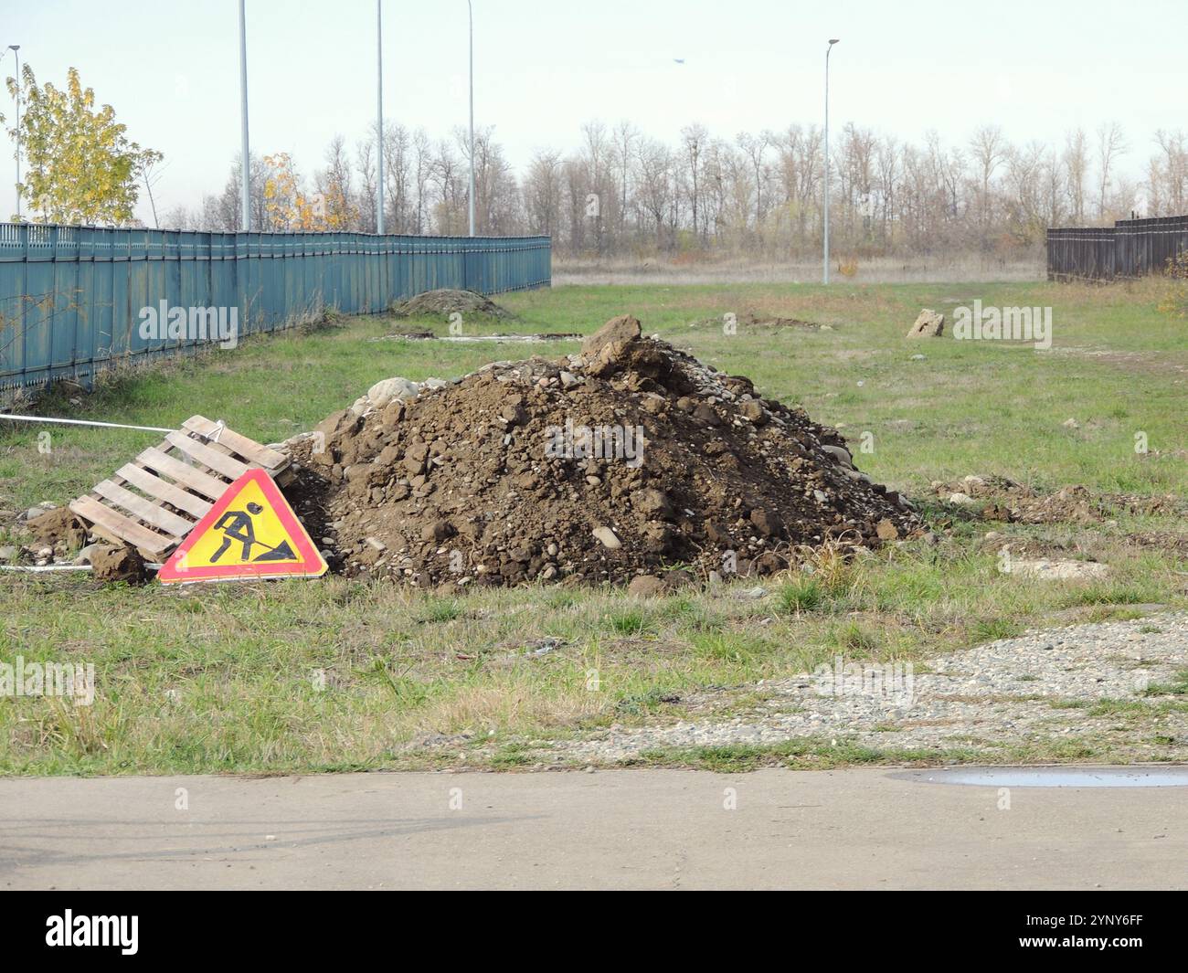 a dug up pile of earth on a green field between two fences with a road ...