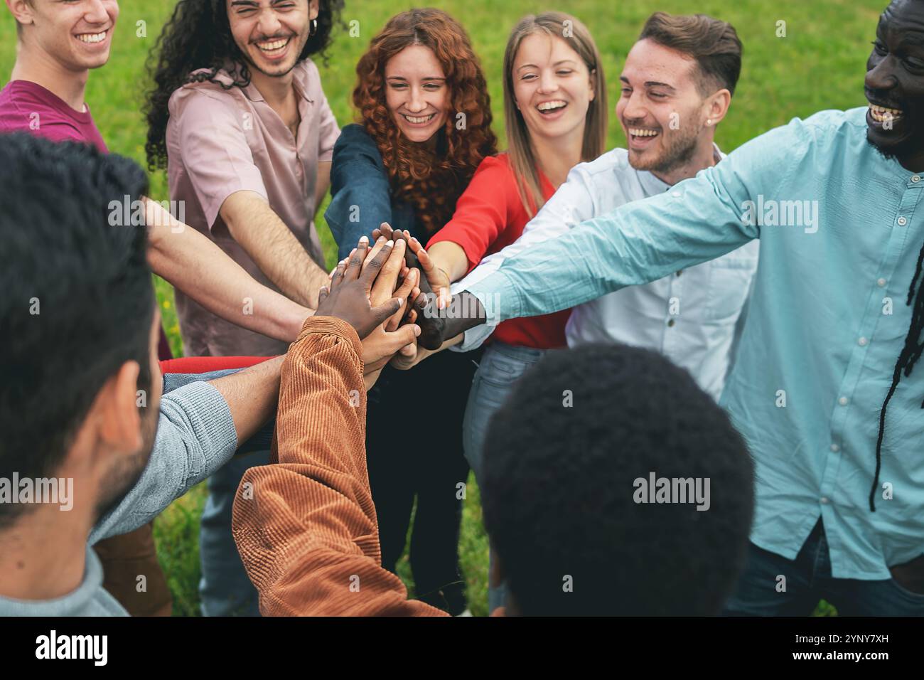 Diverse young team members joining hands in unity circle outdoors. Genuine moment showing mixed ...