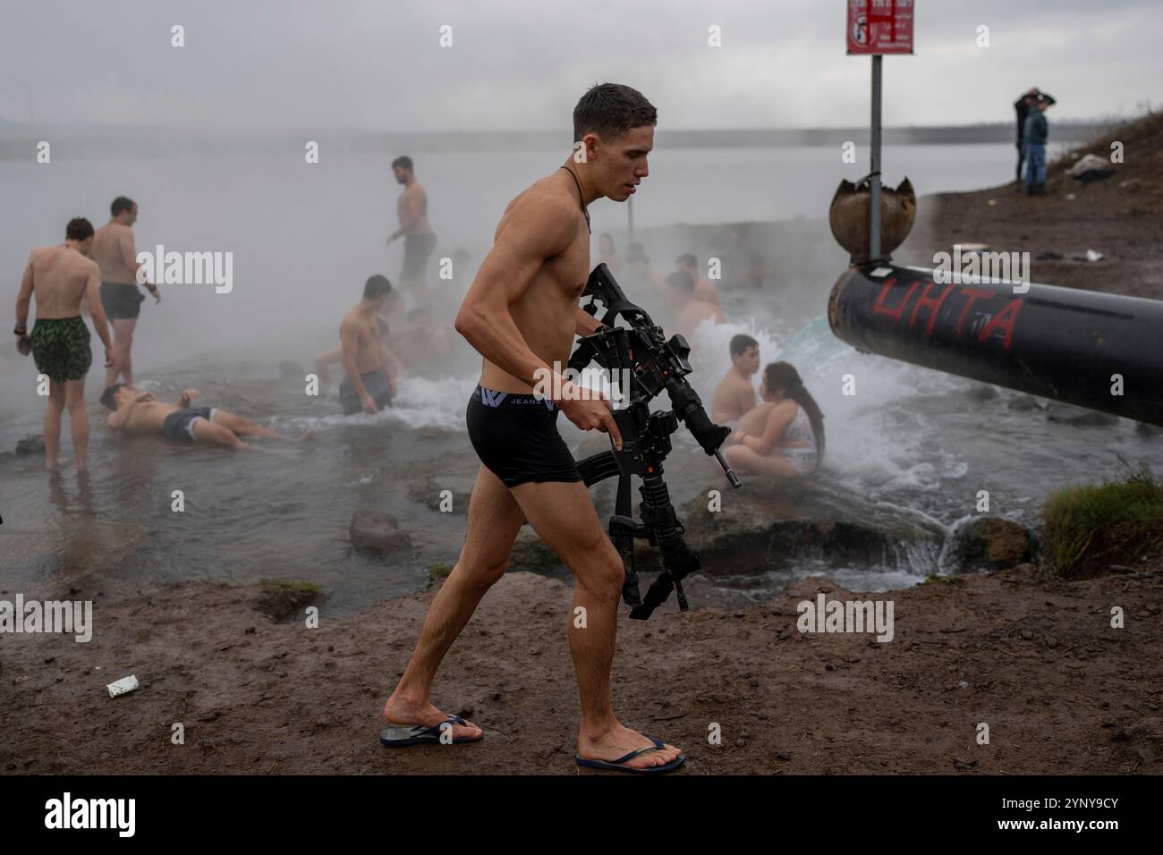 An Israeli soldier holding his weapon bathes with residents in a hot ...