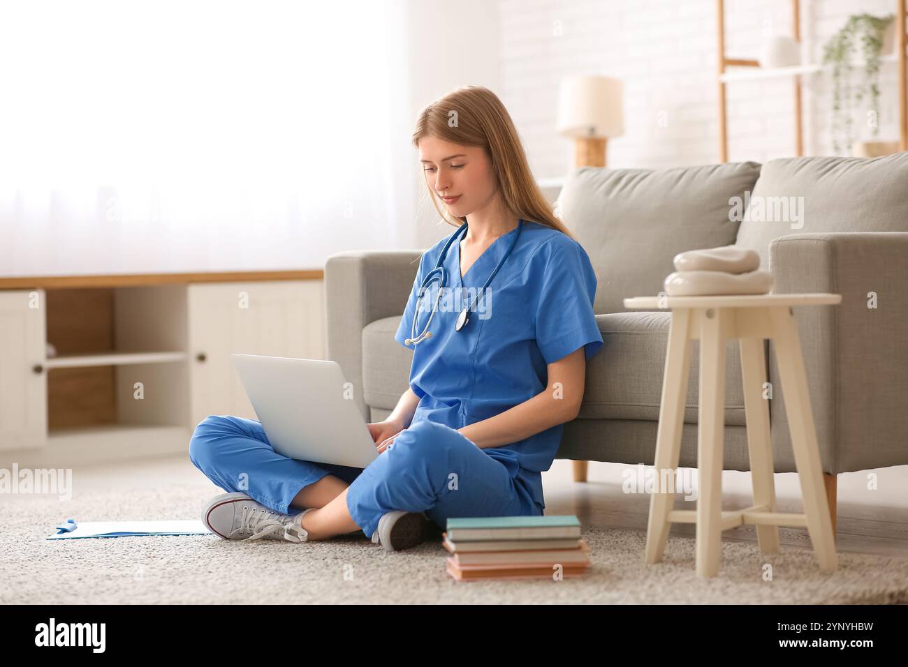 Female medical intern with laptop and books on floor in living room ...