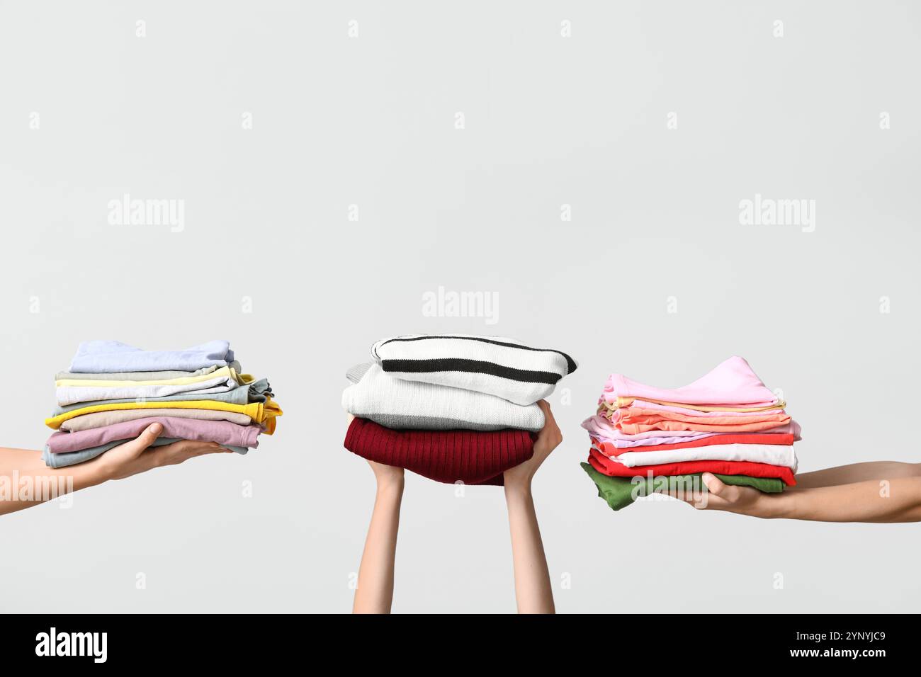 Many female hands with stacks of different clothes on grey background ...