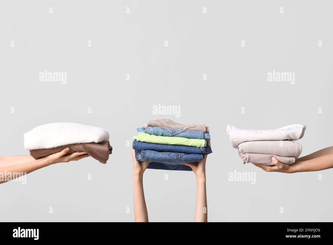 Many female hands with stacks of different clothes on grey background ...