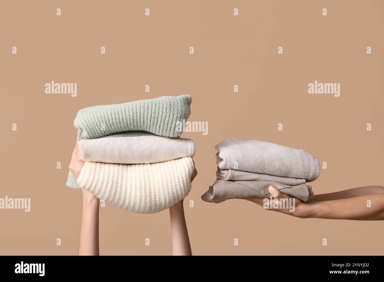 Many female hands with stacks of different clothes on beige background ...