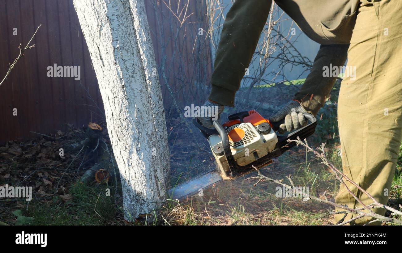 a man in work clothes with an old chainsaw in his hands, bending over ...