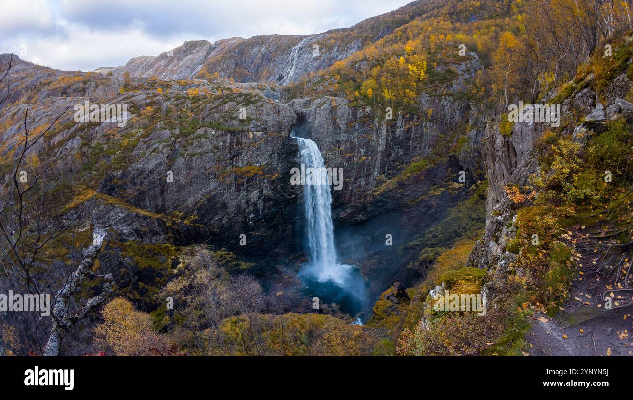 A scenic waterfall cascades down a rocky cliff surrounded by autumn ...