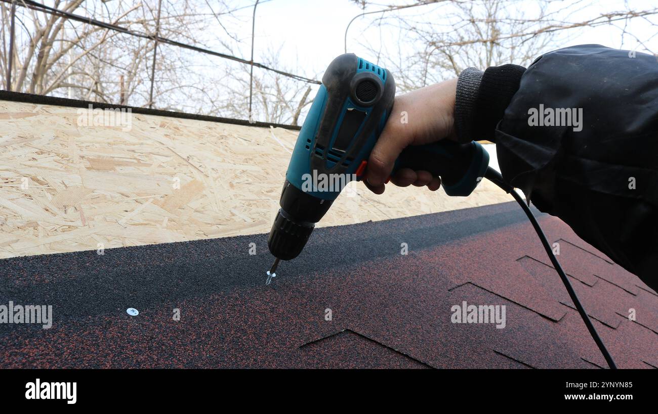 a hand in warm work clothes with a blue electric screwdriver screws ...