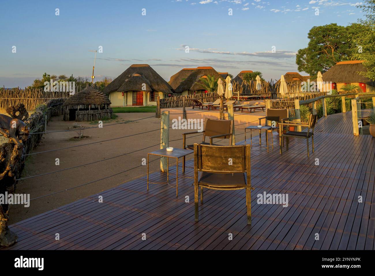Sunset over African lodge with thatched roof huts and wooden terrace in ...