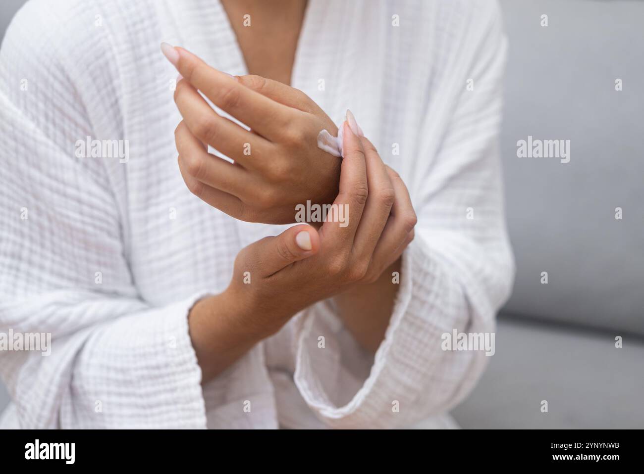 Woman in white gown applying moisturizing lotion on hand on sofa lady ...