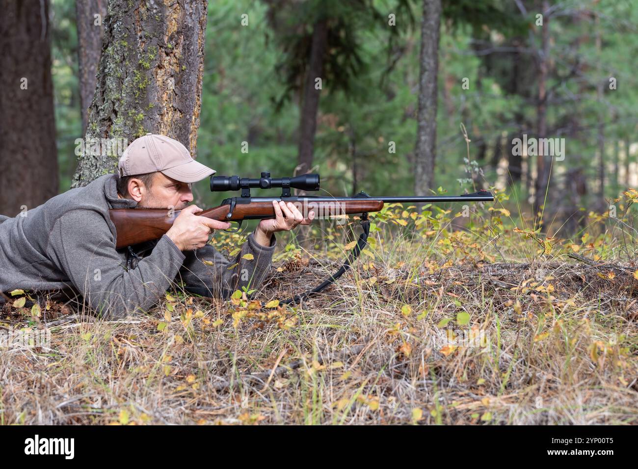 Hunter lies on the ground aiming rifle with the scope at game and ready ...