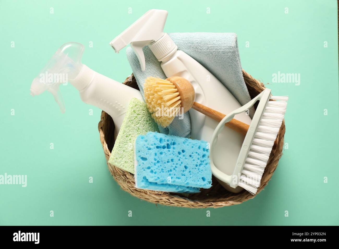 Different cleaning products and tools in wicker basket on turquoise ...