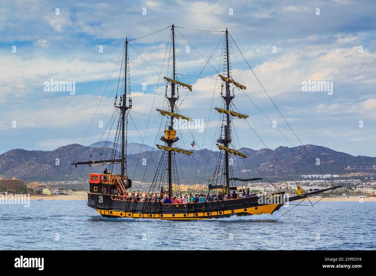 A large ship with a yellow mast sails on the ocean. The ship is filled ...