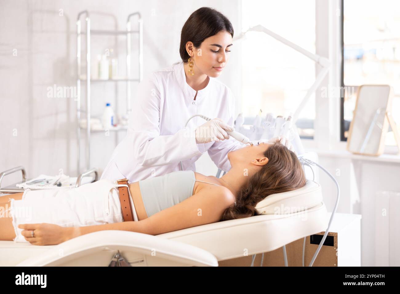 Female cosmetologist performing facial radiofrequency procedure on ...