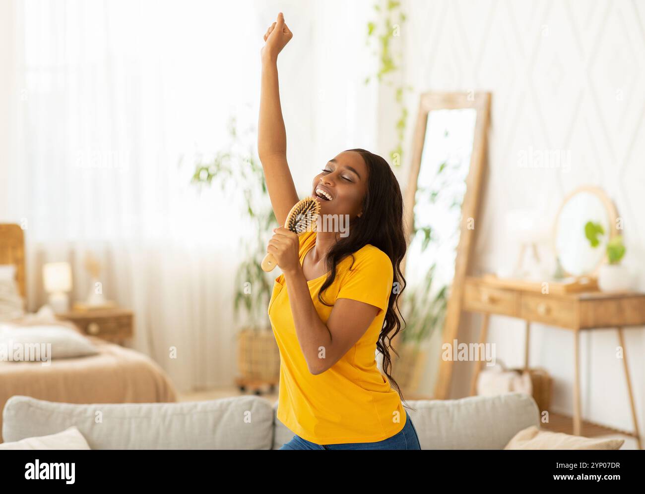 Cheerful black woman with hairbrush as mic singing her favorite song ...