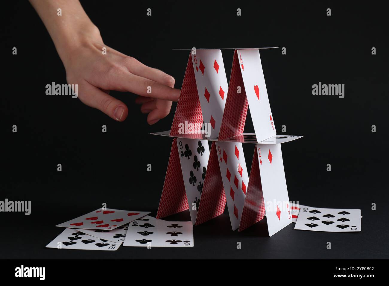 Woman destroying house of playing cards on black background, closeup ...