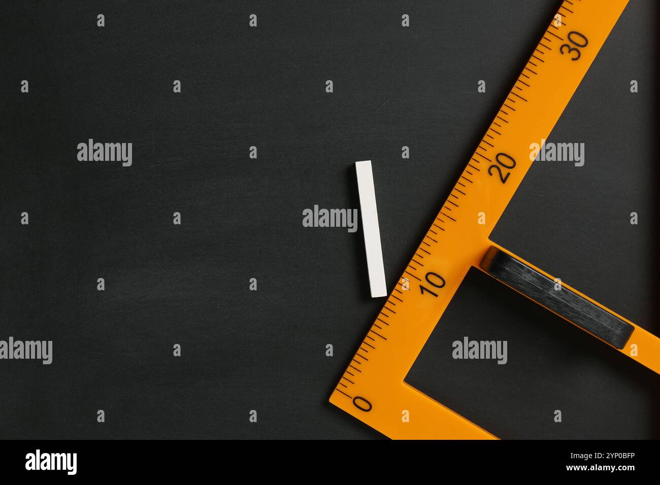 Triangle ruler and chalk on black chalkboard, top view. Space for text ...