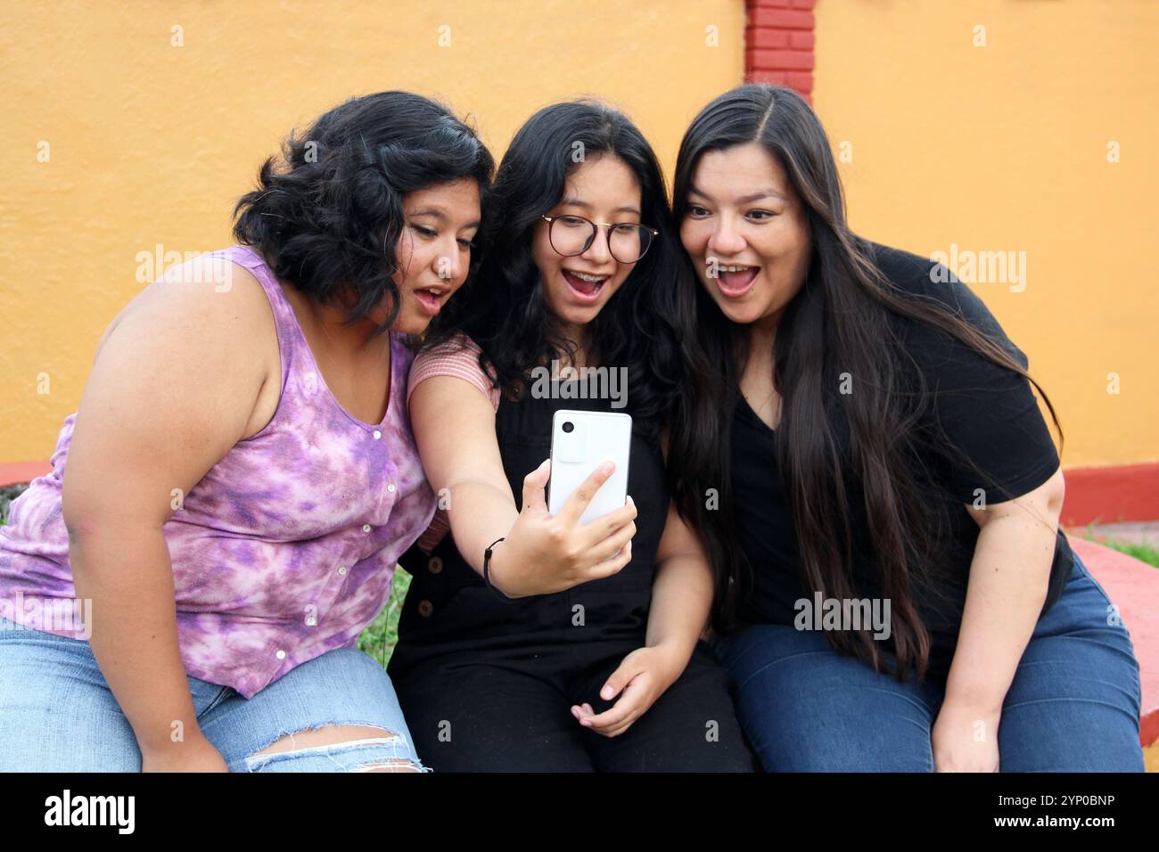 Three brunette Latin women use cell phones to make video calls and take ...