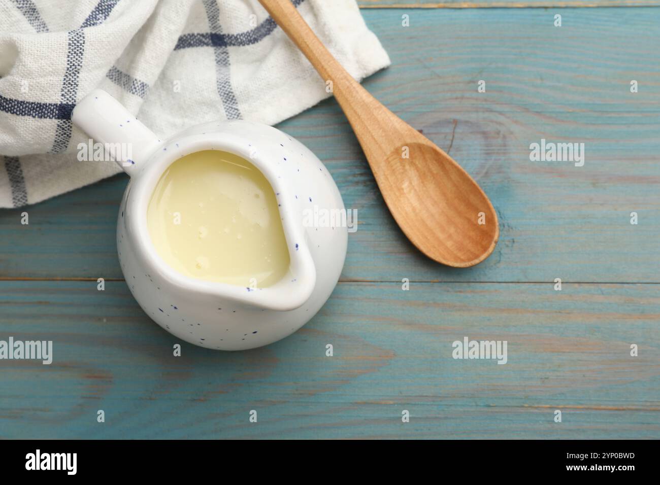 Condensed milk in jug and spoon on light blue wooden table, top view ...