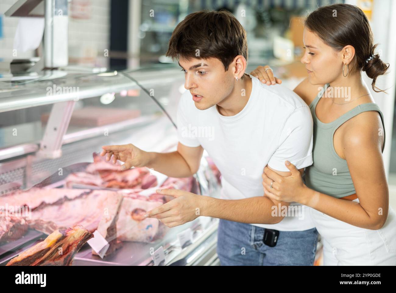 Spouse near butcher shop window inspects goods and choose piece of beef ...