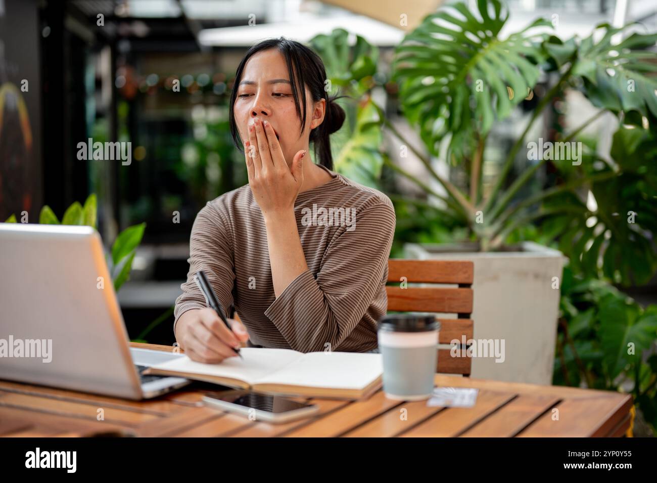 A sleepy, tired Asian woman yawns while working on her laptop or ...