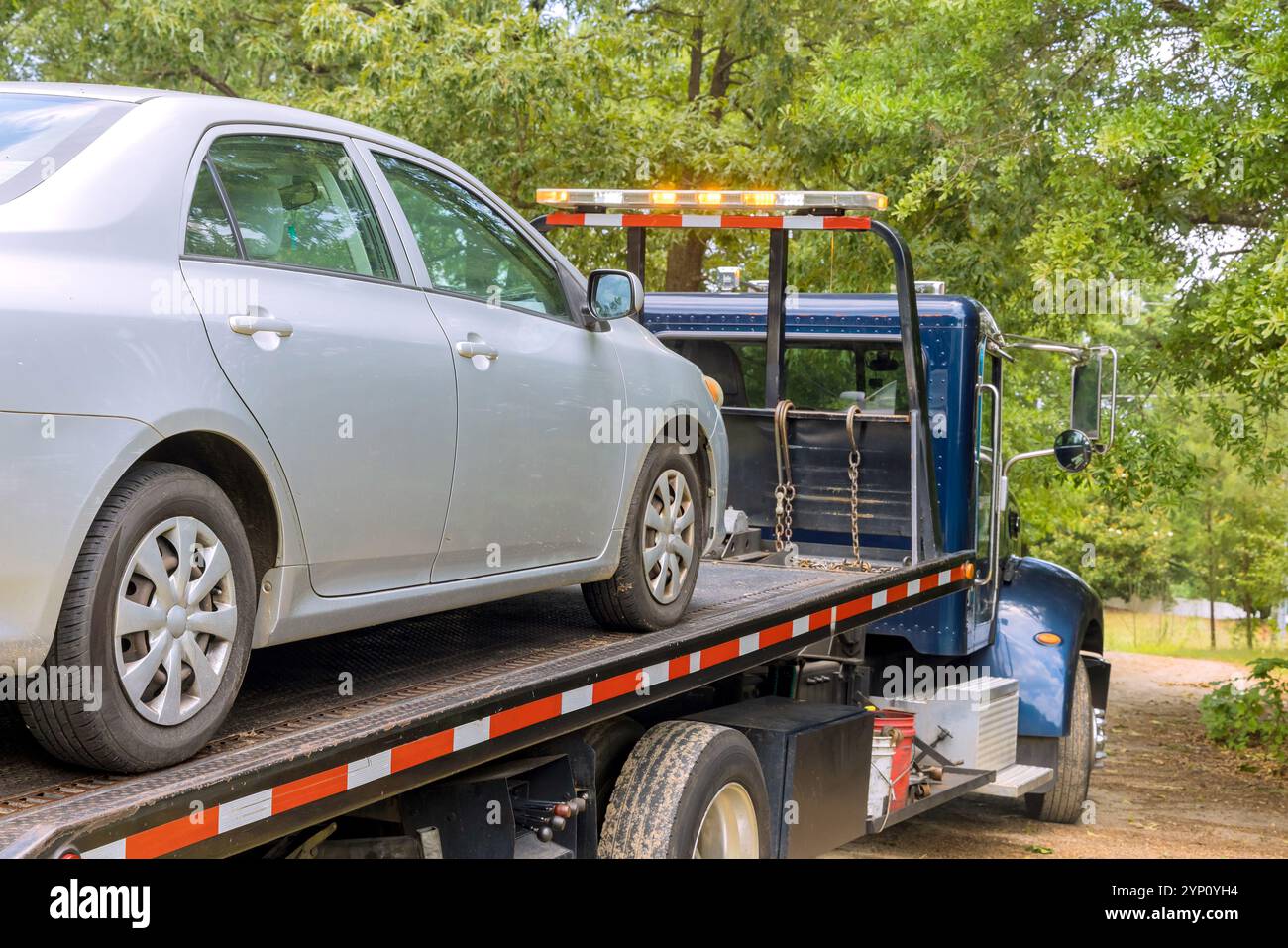 Silver sedan is being loaded onto tow truck in wooded area during truck ...