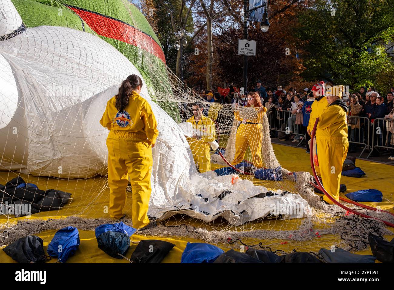 A balloon team dressed in yellow work on inflating Snoopy as the crowd ...