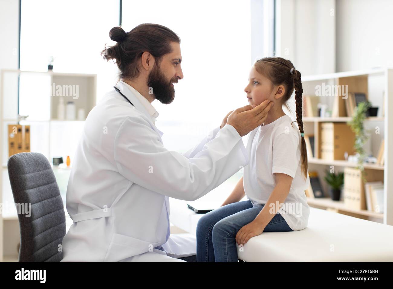 Caucasian male doctor examines throat of young girl in clinical setting. Doctor checks for ...