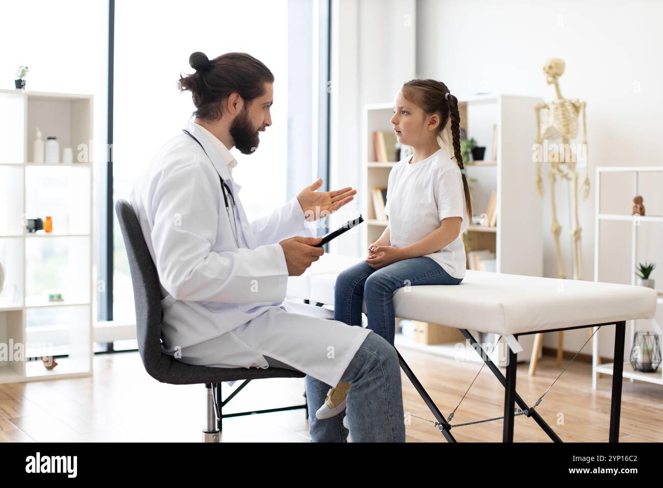 Male doctor examines young Caucasian girl sitting on medical couch ...
