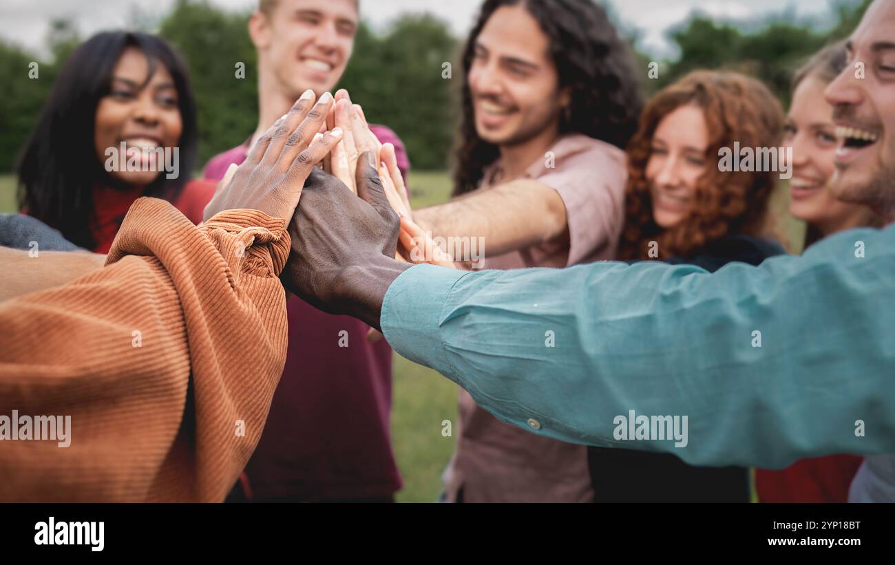 Multiethnic group of young people stacking hands together outdoors, celebrating diversity and ...