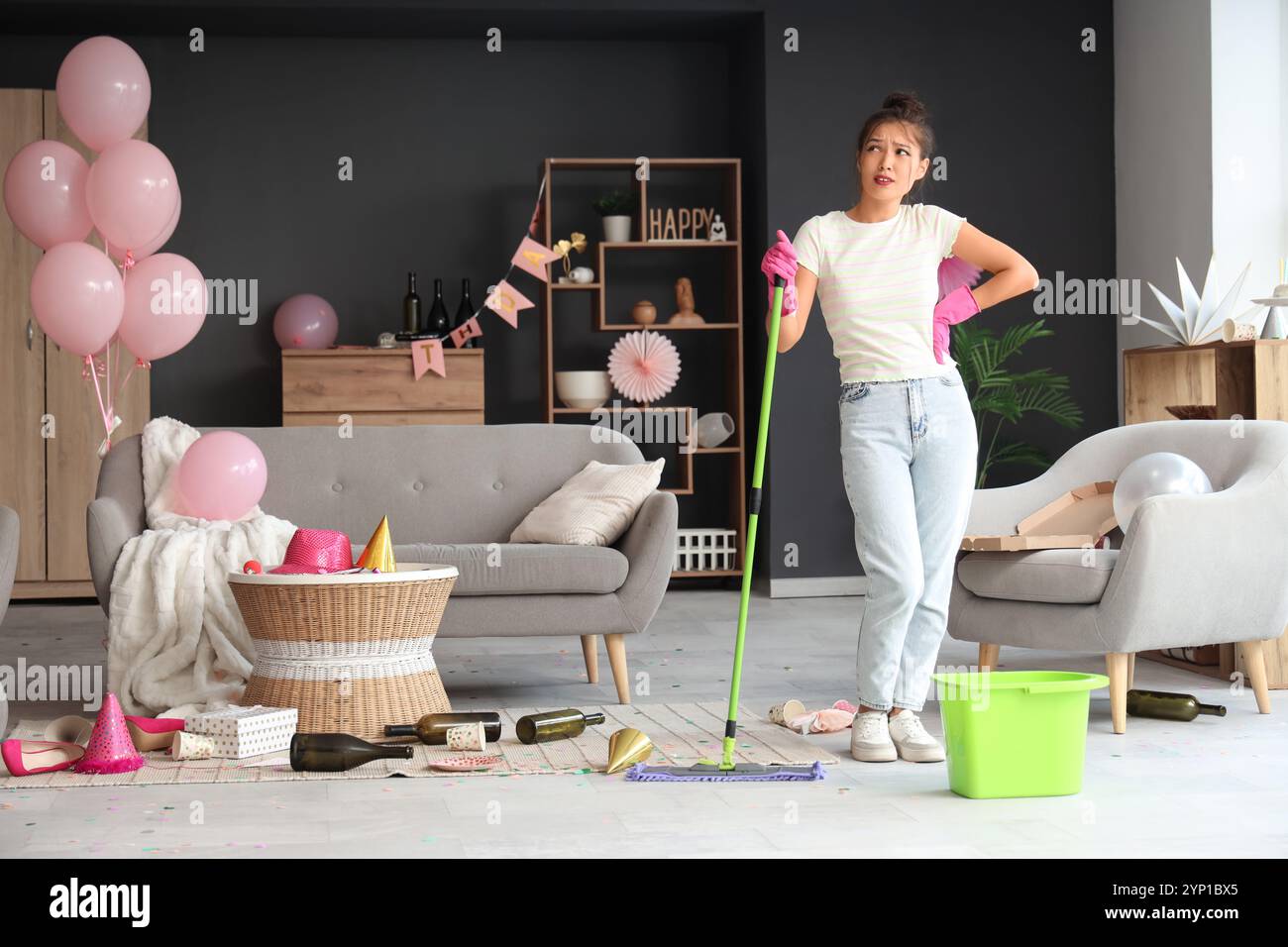 Displeased young Asian woman with mop in messy room after Birthday ...