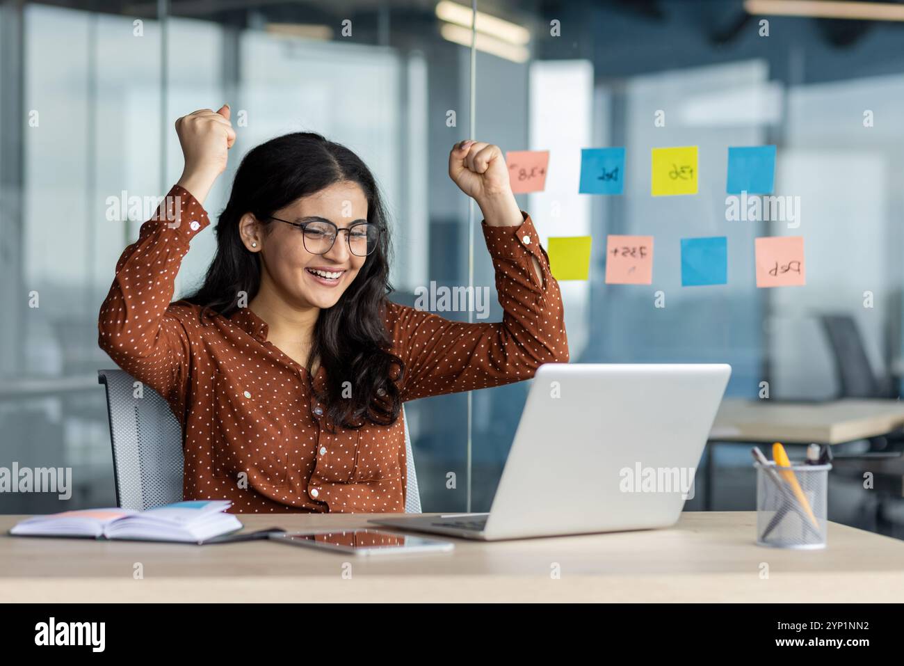 Hispanic woman businesswoman happily celebrates success at office desk ...