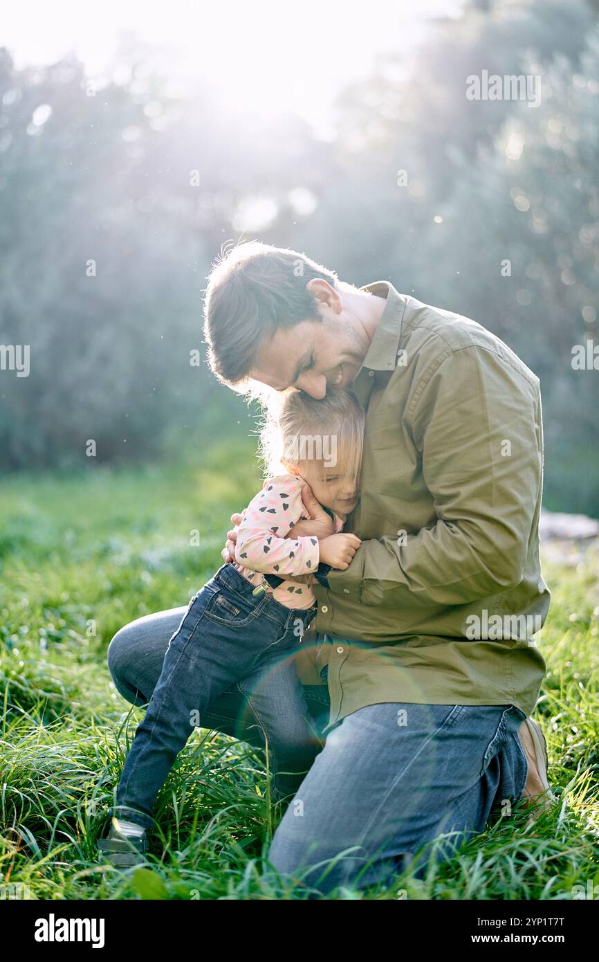 Smiling dad hugging little girl sitting on his knees on the lawn Stock Photo - Alamy